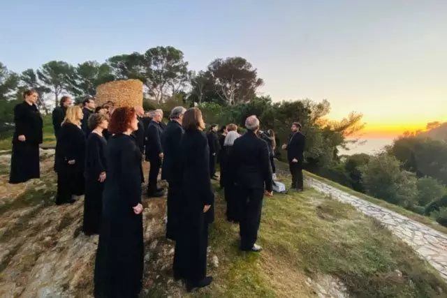 Beberapa orang berpakaian serba hitam berdiri bersama di puncak bukit dengan latar belakang matahari terbenam atau matahari terbit.