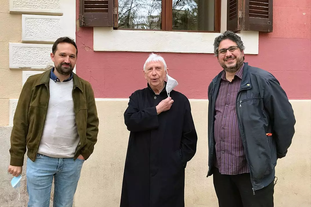 Tres hombres con abrigos posan afuera, sosteniendo o quitándose las máscaras faciales.