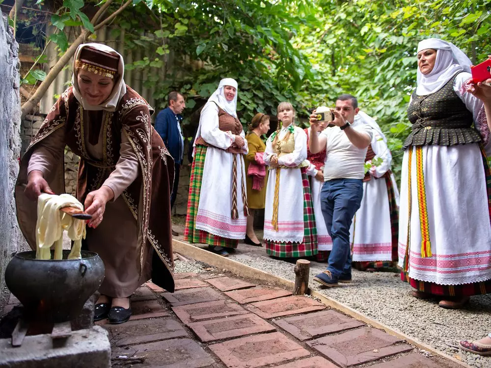 'n Vrou wat tradisionele Armeense drag dra, buk af om na 'n buitestoof te kyk terwyl sy 'n maaltyd voorberei.