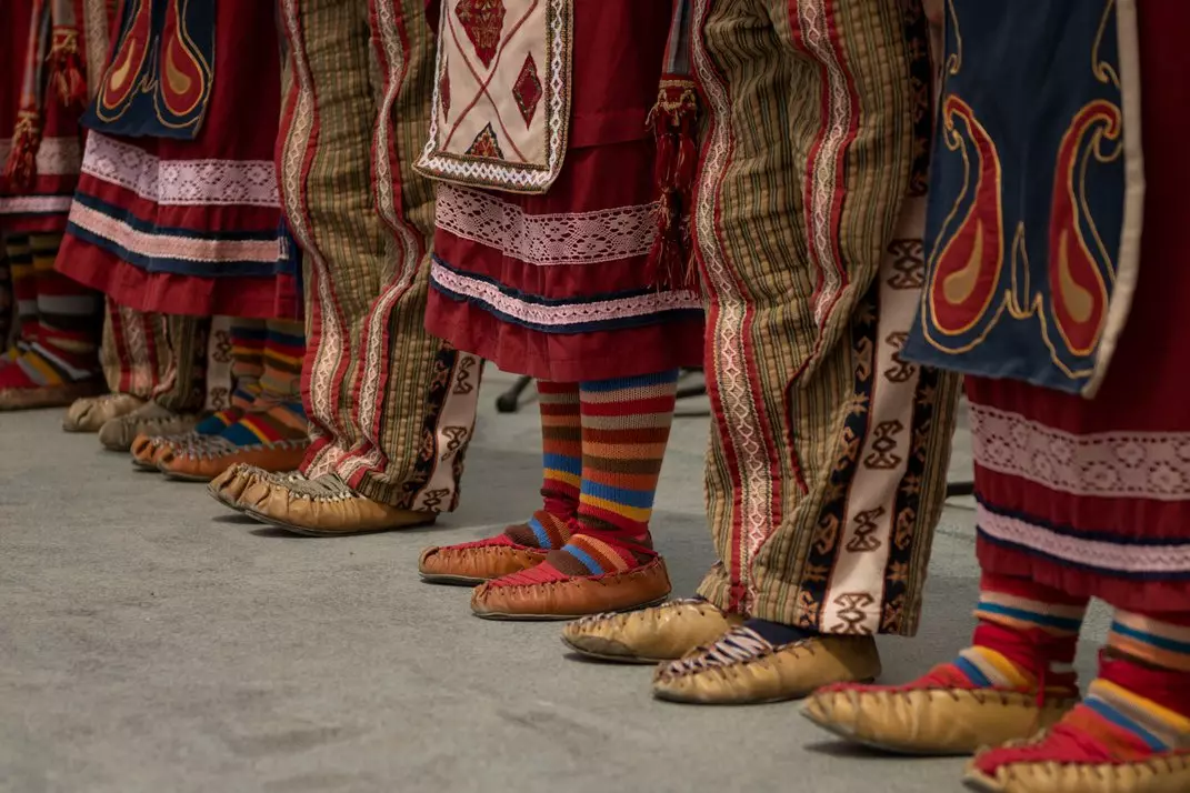 People wearing traditional, Armenian shoes with brightly colored pants and socks stand in a line. They are pictured from the waist down.