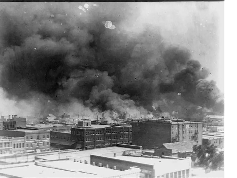 Черно-бяла снимка на сгради от въздушна перспектива, с гъсти струйки черен дим, издигащи се над и закриващи небето
