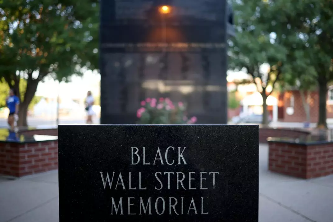 Открит паметник на жертвите на клането; на преден план, черна плоча с гравирани надписи BLACK WALL STREET МЕМОРИАЛ; на заден план висока мраморна конструкция с имена, гравирани върху черен камък