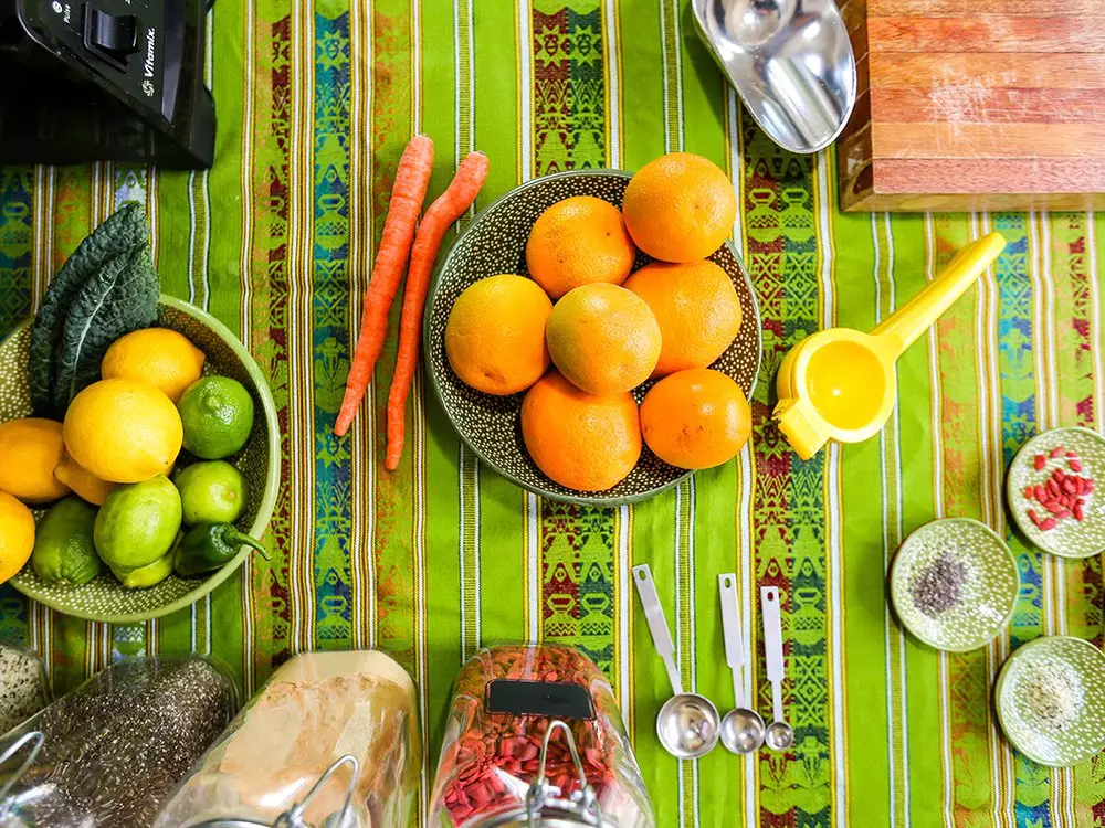 Ciotole di agrumi, tra cui limoni, lime e arance, sono disposte su una tovaglia a strisce verde brillante. Dietro le ciotole ci sono barattoli pieni di vari super alimenti tra cui le bacche di Goji.