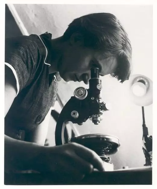 Schwarz-Weiß-Foto einer Frau, die in ein Mikroskop blickt.