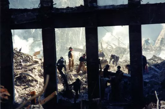 工人在 2001 年 9 月 11 日的照片，从部分被毁的建筑物的柱子中看到的破坏堆。他们穿着安全帽和制服。烟雾在这里和那里升起。