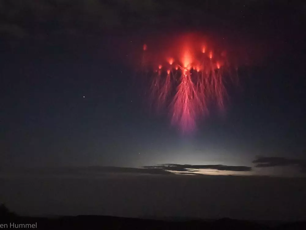 Un nuage de lumière rouge est suspendu dans les nuages avec des tentacules d'éclairs rouges suspendus en dessous.