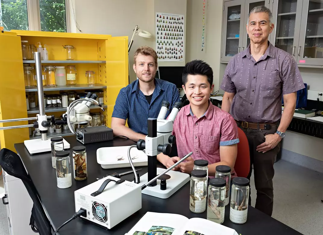 Drie wetenskaplikes by 'n werkbank met 'n mikroskoop in 'n laboratorium