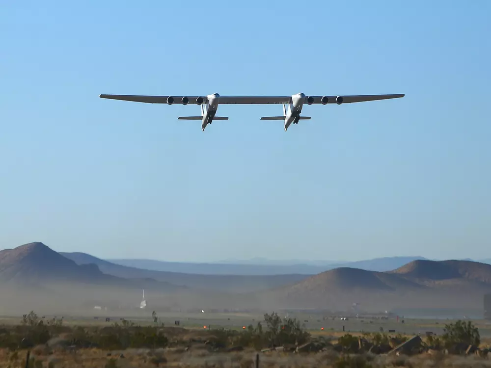 这架 385 英尺宽的大鹏飞机在沙漠上空湛蓝的天空中飞行，地平线上的山脉