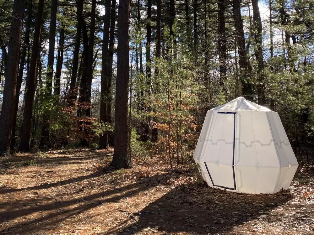 Ett vitt oktogonformat origamitält sitter i skogen i New England
