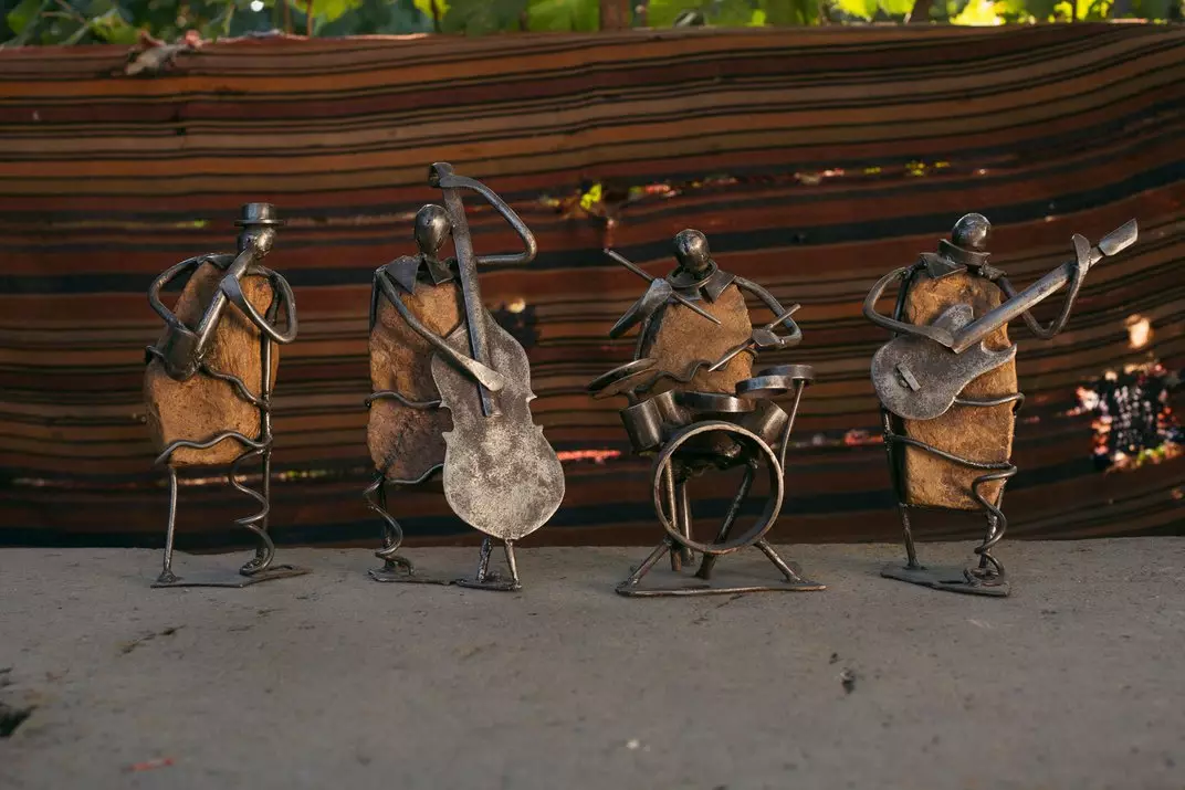 Quatro esculturas de metal de figuras humanas tocando instrumentos estão posicionadas uma ao lado da outra.