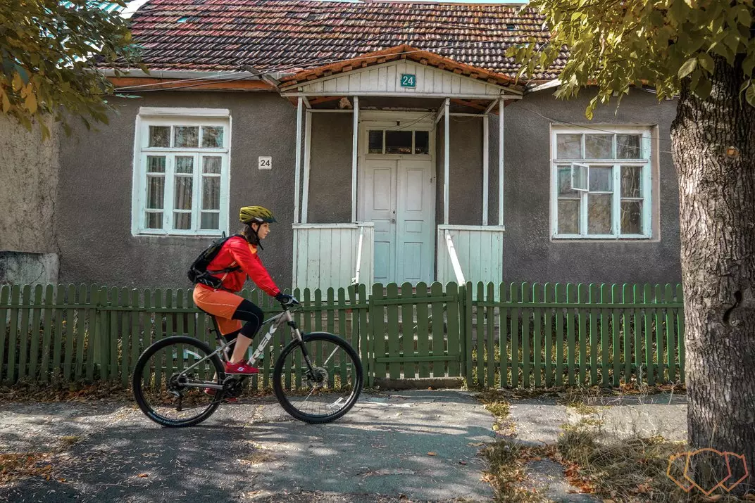Une jeune femme fait du vélo devant une maison arménienne traditionnelle.