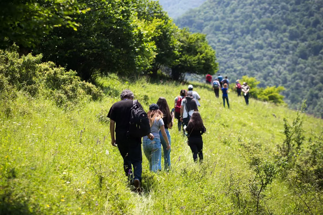 Een groep wandelaars loopt door een veld richting een berg, met hun ruggen weg van de camera.