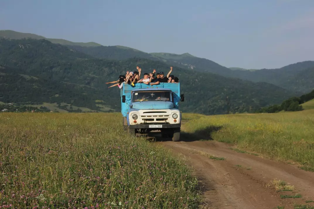 Modri tovornjak, poln ljudi, vozi skozi zeleno polje.