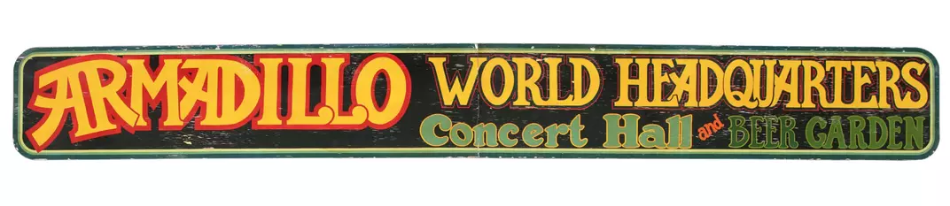 ປ້າຍທີ່ແຕ້ມດ້ວຍມືເປັນສີແດງ, ສີເຫຼືອງ, ສີຂຽວ ແລະສີດຳ ທີ່ຂຽນວ່າ ARMADILLO World Headquarters Concert Hall ແລະ Beer Garden