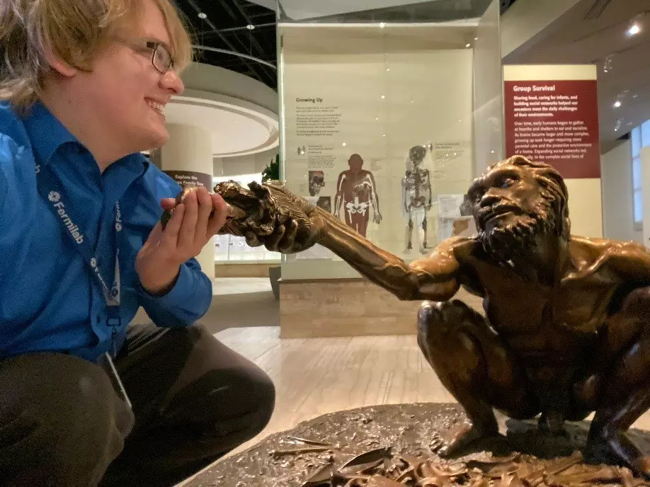 Ein Besucher geht in die Hocke, um einen bronzenen Fisch zu nehmen, der von einer lebensgroßen Bronzestatue des Homo heidelberensis angeboten wird, die im ausgestellt ist