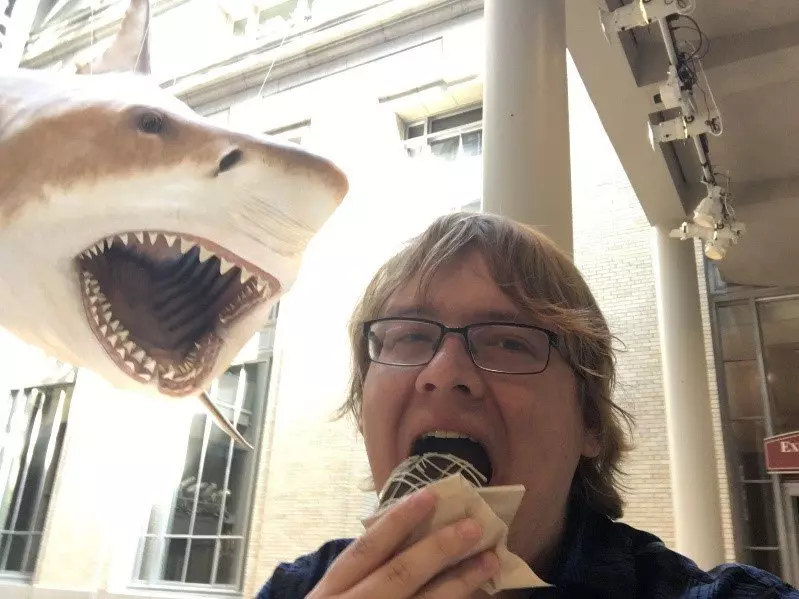 E Besucher ësst e Pâtisserie wärend e Selfie virun dem 52-Fouss Megalodon Modell am Ocean Terrace Café am Smithsonian National Museum of Natural History ausgestallt gëtt.