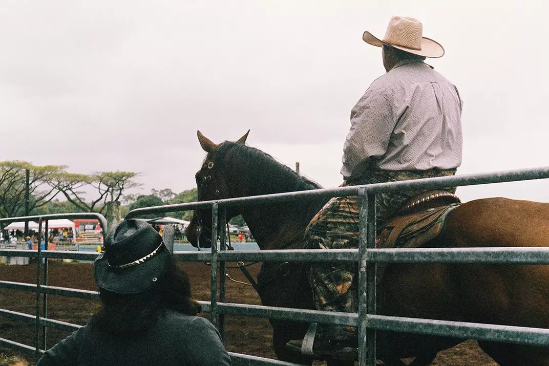 Een persoon met een cowboyhoed zit bovenop een paard en staat naast een andere persoon met een cowboyhoed aan de andere kant van een poort.