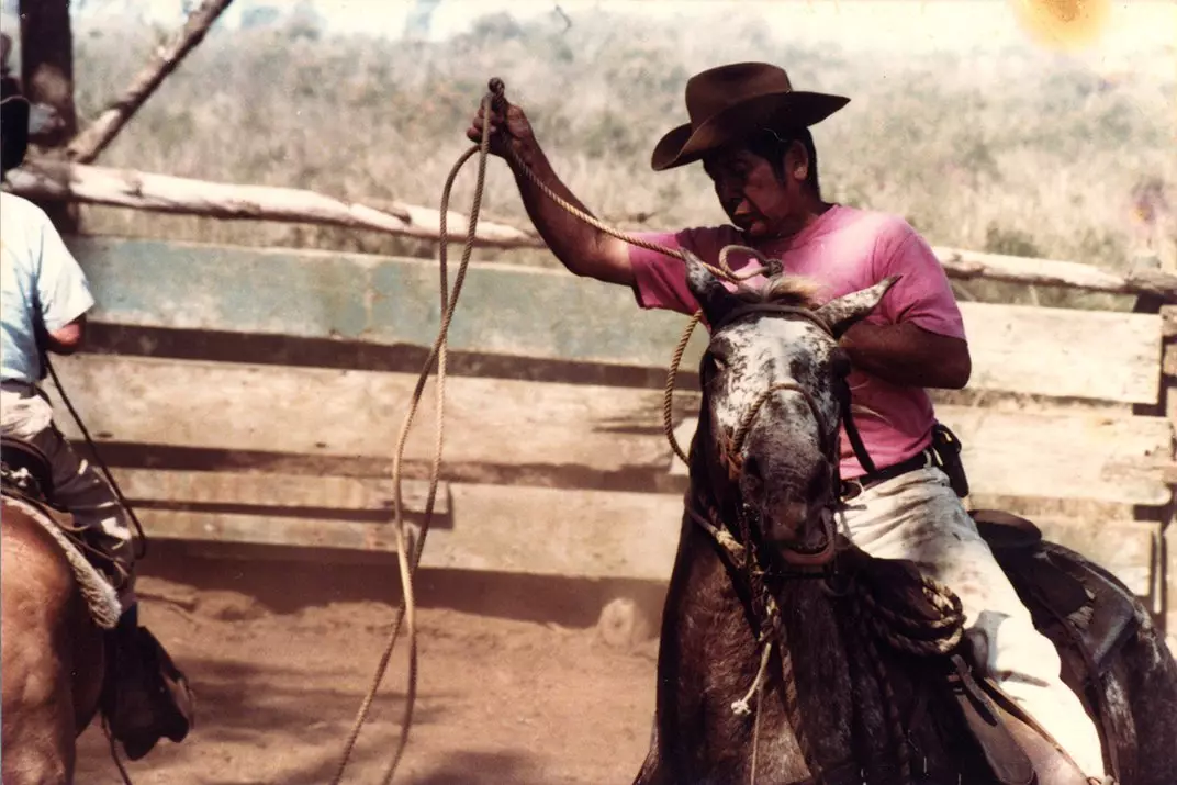 카우보이 모자와 분홍색 셔츠를 입은 남자가 말 위에 앉아 있습니다. 말의 얼굴이 일그러져 있습니다.