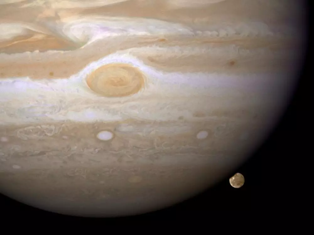 Abarcando la mayor parte de la imagen está el planeta Júpiter, con su mancha roja en el centro. En la parte inferior derecha, su luna más grande, Ganímedes, alcanza su punto máximo detrás del planeta.