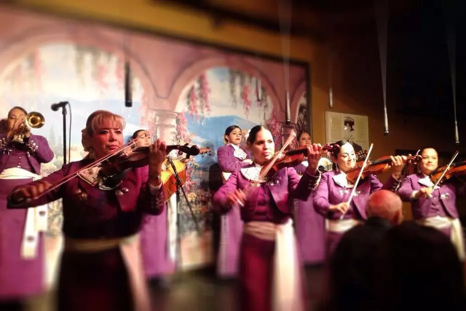 Gyrmyzy we ak däp bolan eşiklere laýyk geýnen Mariachi zenanlarynyň hemmesi, ummanyň garşysynda ýerleşýän arçany şekillendirilen boýalan heýkeliň öňünde bilelikde çykyş edýär.