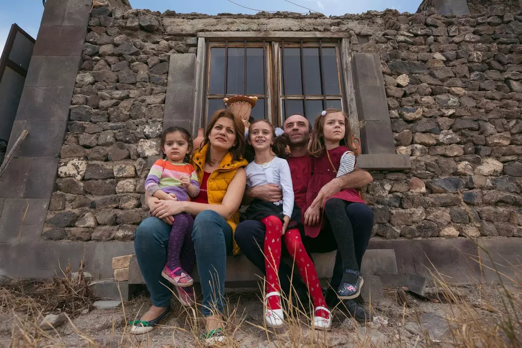 Zilamek û jina xwe li ber dîwarekî kevirî rûniştine, sê keçên wan ên ciwan di hembêza wan de rûniştine.