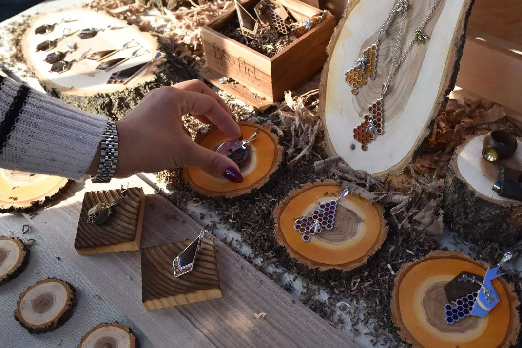 Vários colares com motivos de favos de mel são exibidos em pequenos pedaços circulares de madeira.