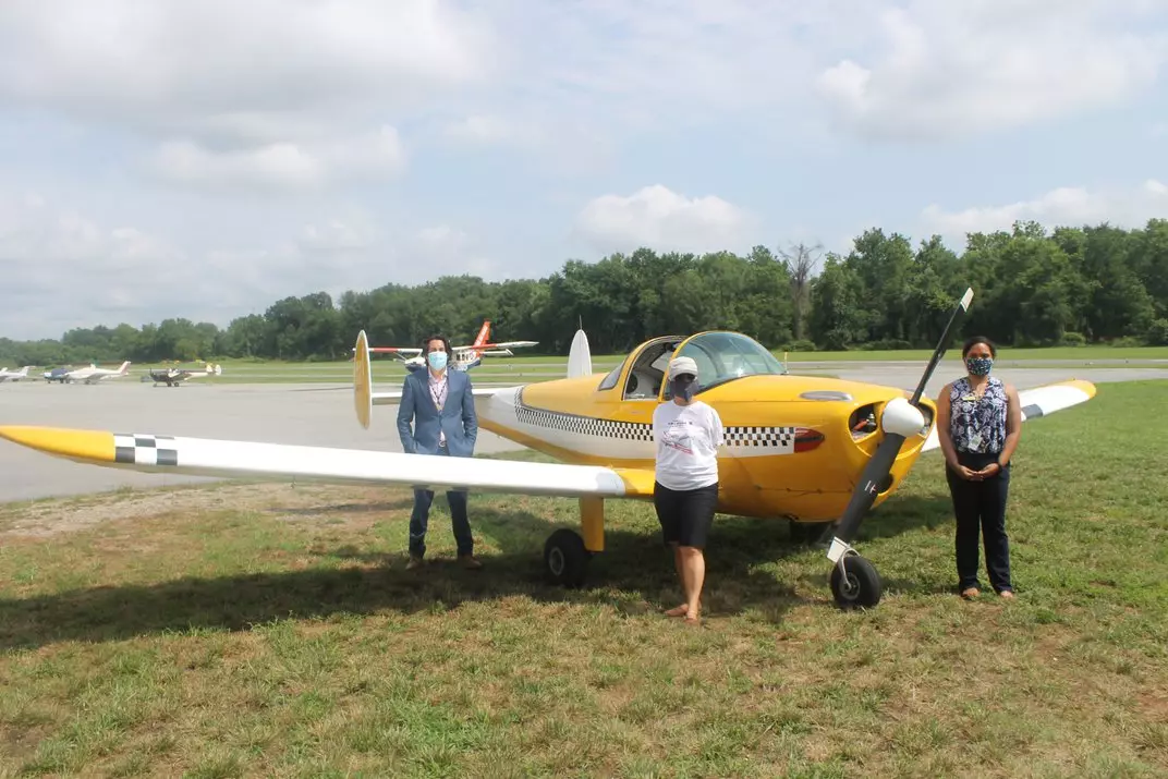 تین لوگ پیلے رنگ کے ہوائی جہاز کے سامنے کھڑے ہیں۔