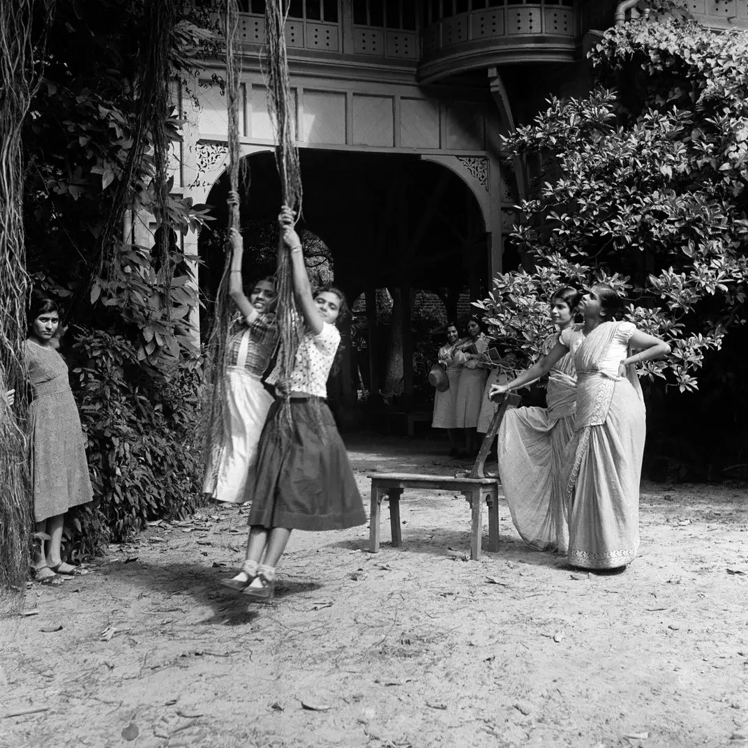 Une image en noir et blanc d'écolières en saris et uniformes jouant sur des balançoires dans une cour