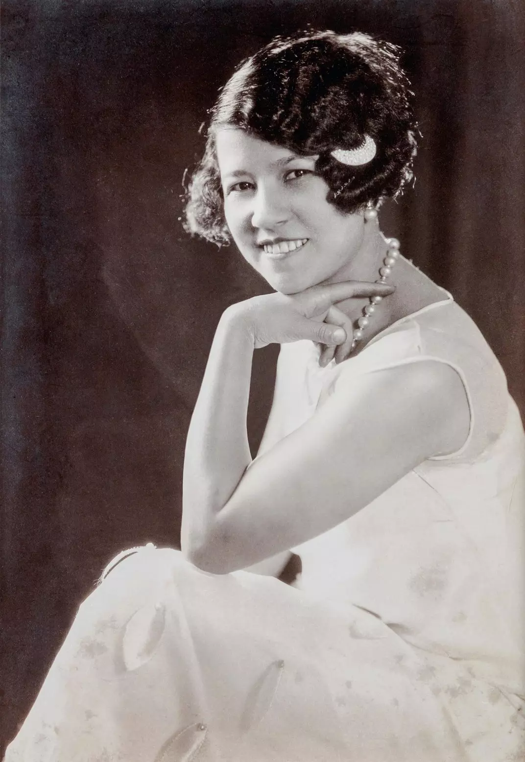 Um retrato de estúdio posado de Collins, uma mulher negra com cabelo curto recortado em pérolas e um elegante vestido branco