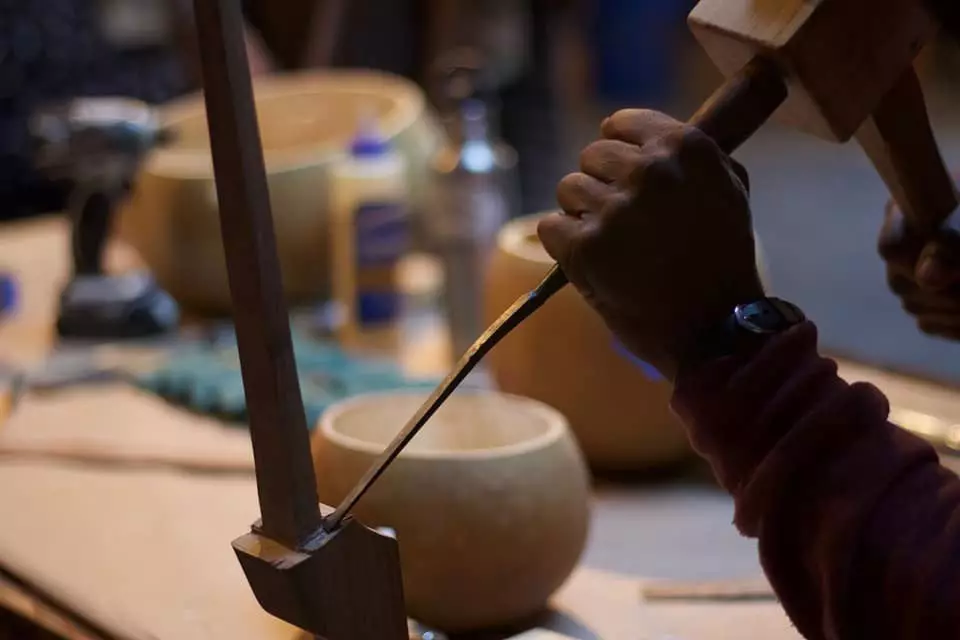 Primo piano su un paio di mani che cesellano un pezzo di legno.