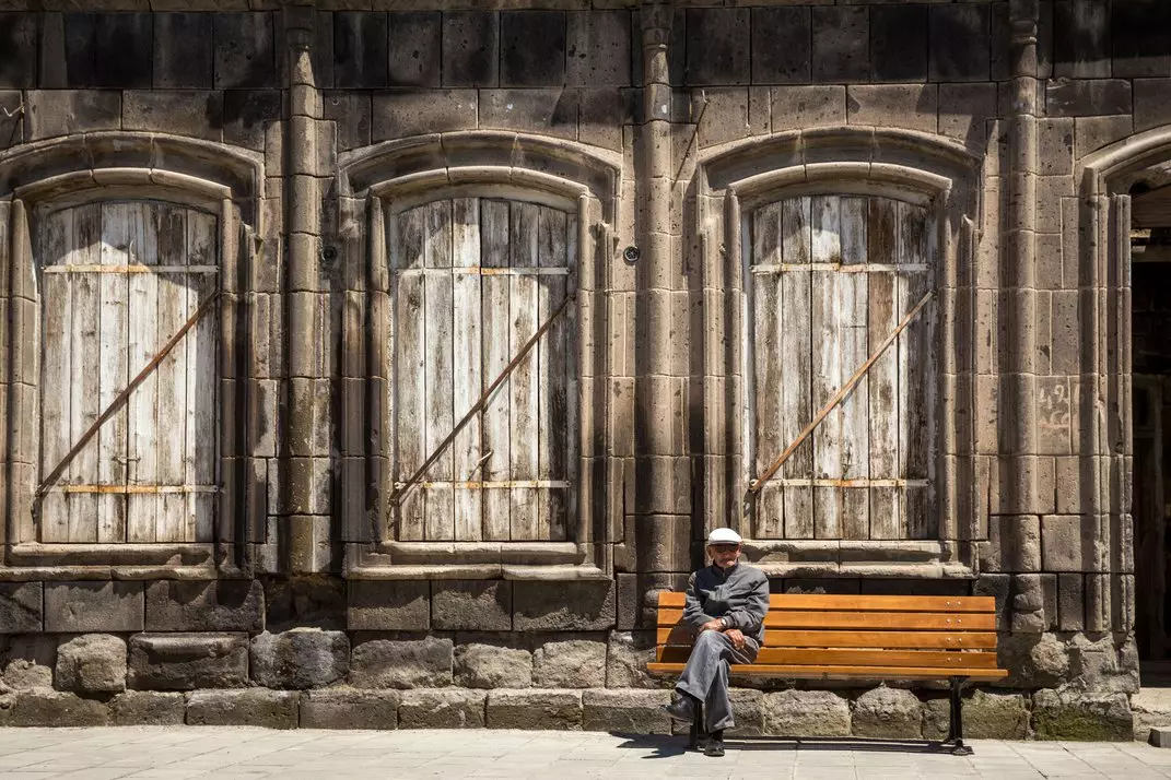 Un home senta diante dun muro de pedra gris escuro con tres portas señoriais de madeira.