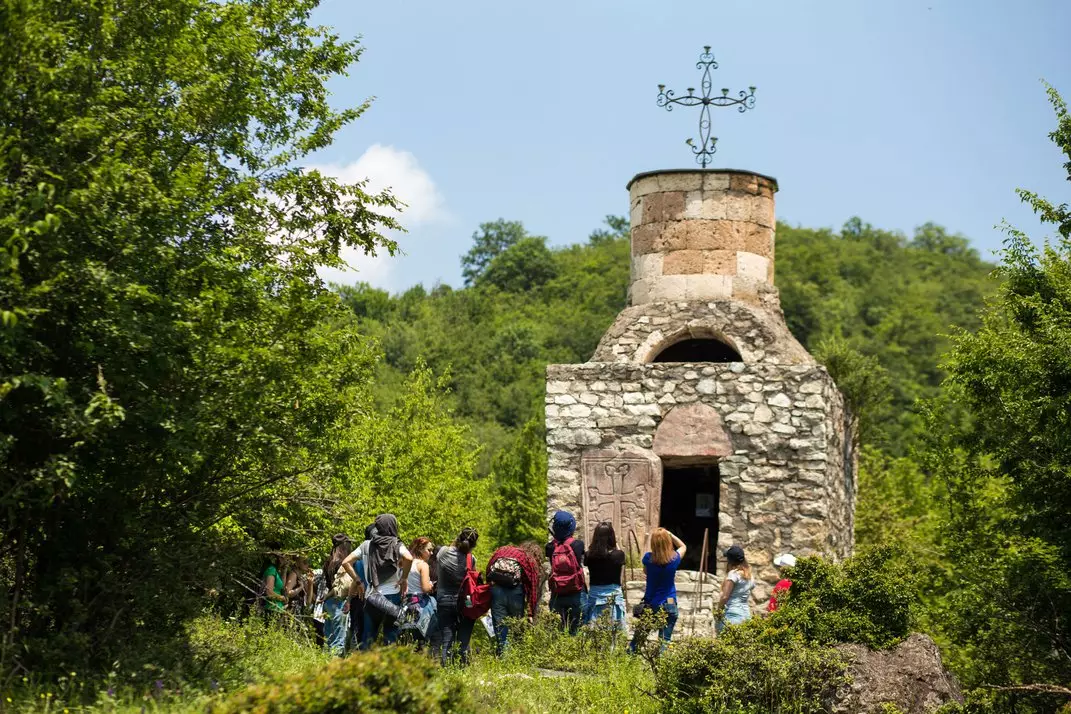 V gozdu stoji majhna kamnita kapelica. Obkrožena je s turisti, ki fotografirajo.