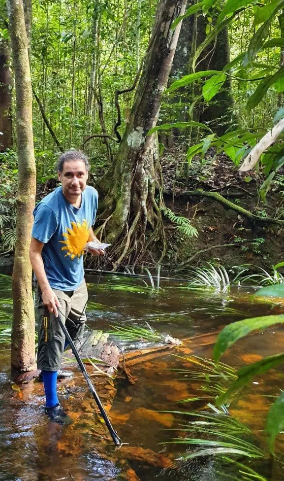 Un hombre se para con un palo en aguas poco profundas.