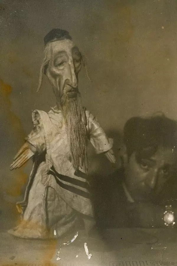 Սեպիայի տոնով լուսանկարում պատկերված է ռաբբիի ձեռագործ տիկնիկը: Հետին պլանում կտրված, մուգ մազերով տղամարդը կռվում է՝ բռնելով տիկնիկը: