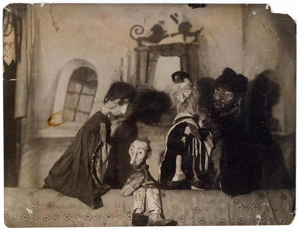 Четыре куклы стоят в центре сцены, демонстрируя декорации маленькой деревни.