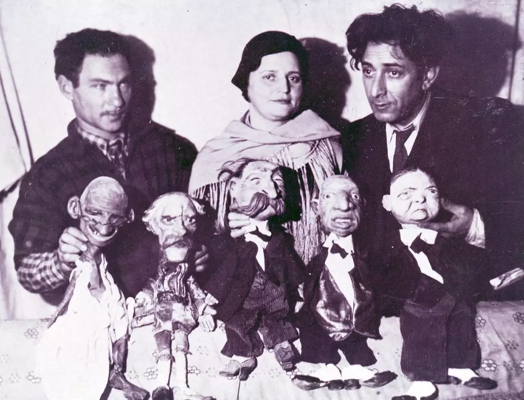 Dos homes i una dona es troben al fons de la foto. Tots ells tenen titelles fets a mà de personatges polítics