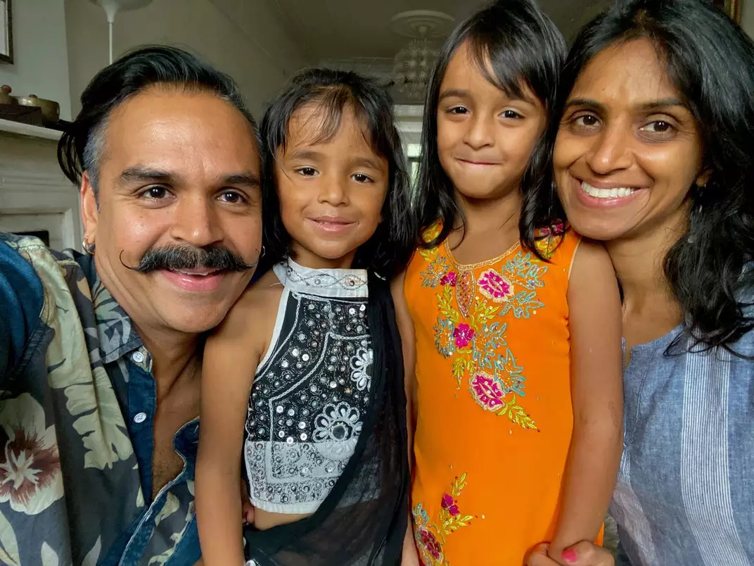 Family selfie, with Sunny Jain (author) on the left with handlebar mustache, gold earring, and blue Hawaiian print shirt. His wife is on the right, with long dark hair and a blue blouse. Their two young daughters are in between, all smiling.