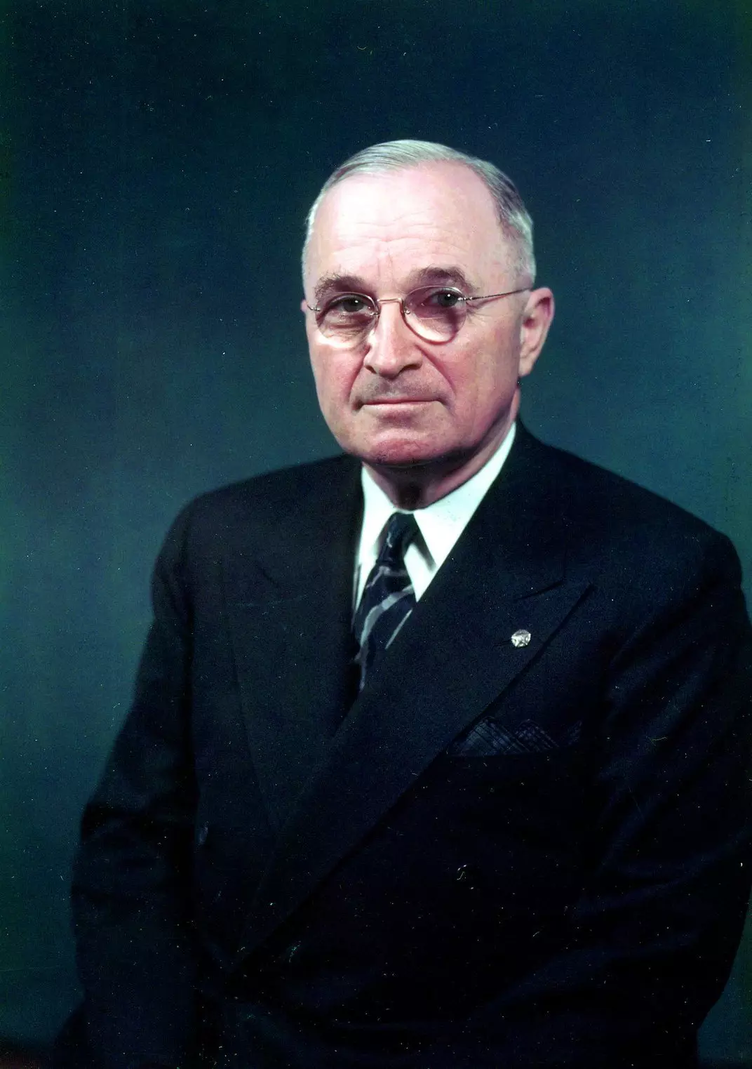 Színes fénykép Trumanról, egy fehér középkorú férfiról, ősz, fésült hajjal, szemüveggel, komoly arckifejezéssel, öltönyben és nyakkendőben