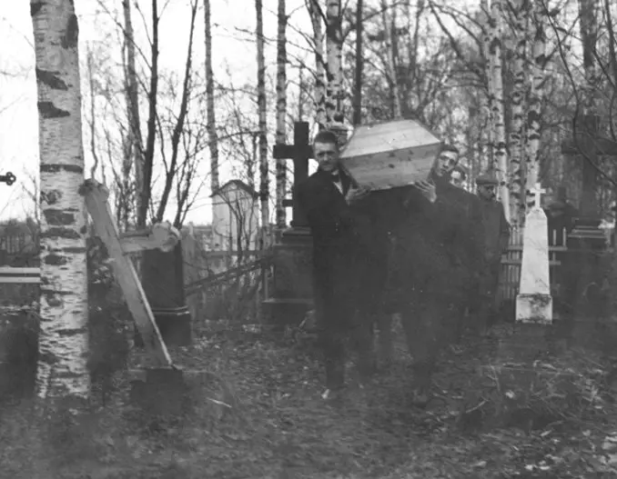 남자들은 자작나무와 키 큰 십자가 묘비 사이에서 관을 나르고 있다