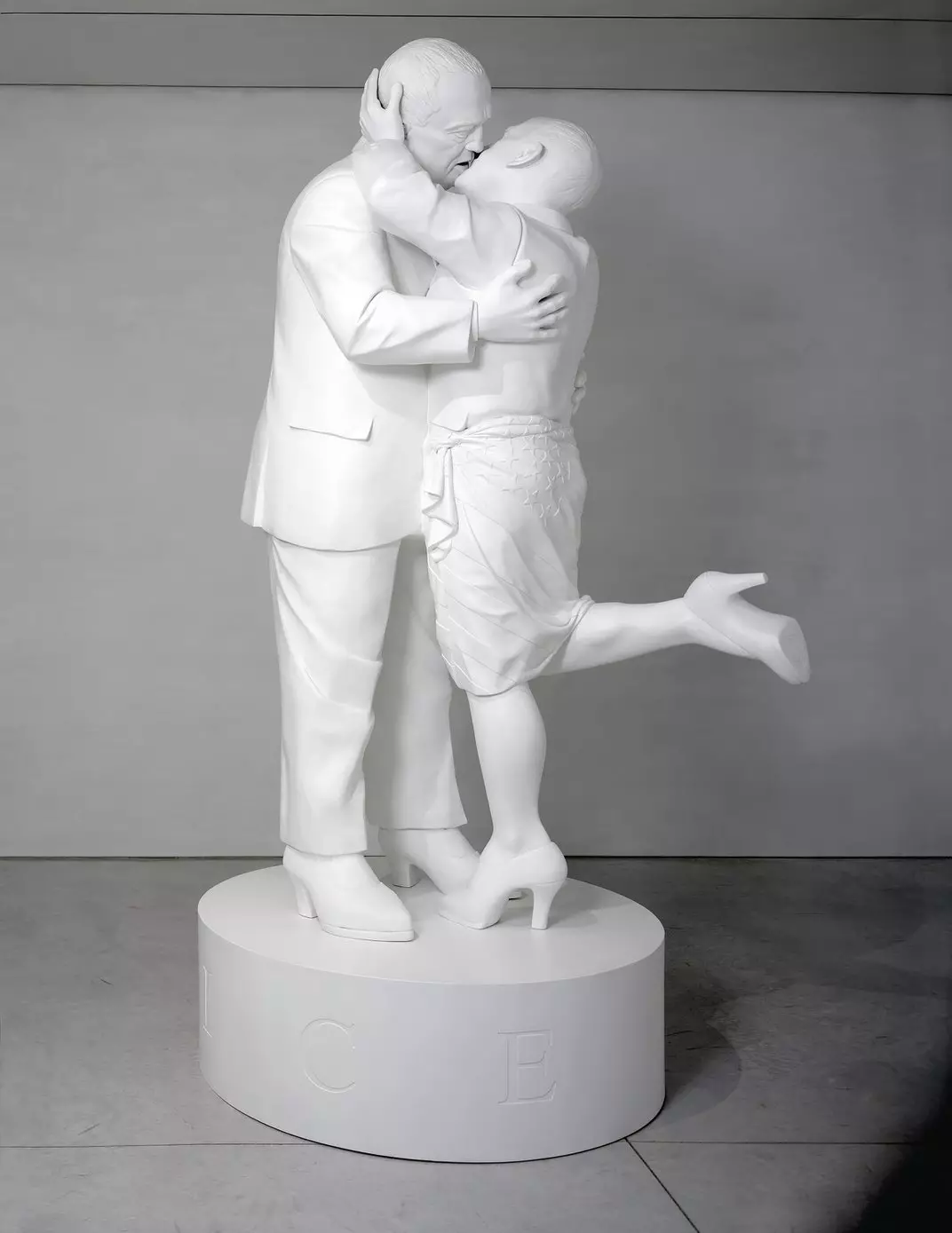 신고전주의 양식의 흰색 동상, 하이힐과 양복을 입은 두 남자가 키스하고 있습니다.