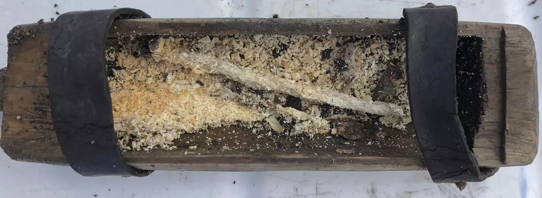 A téglalap alakú doboz belső képe, amely tele van egy hosszú, vékony, kúpos gyertyához hasonlóval, körülvéve morzsolódott megsárgult méhviaszdarabokkal