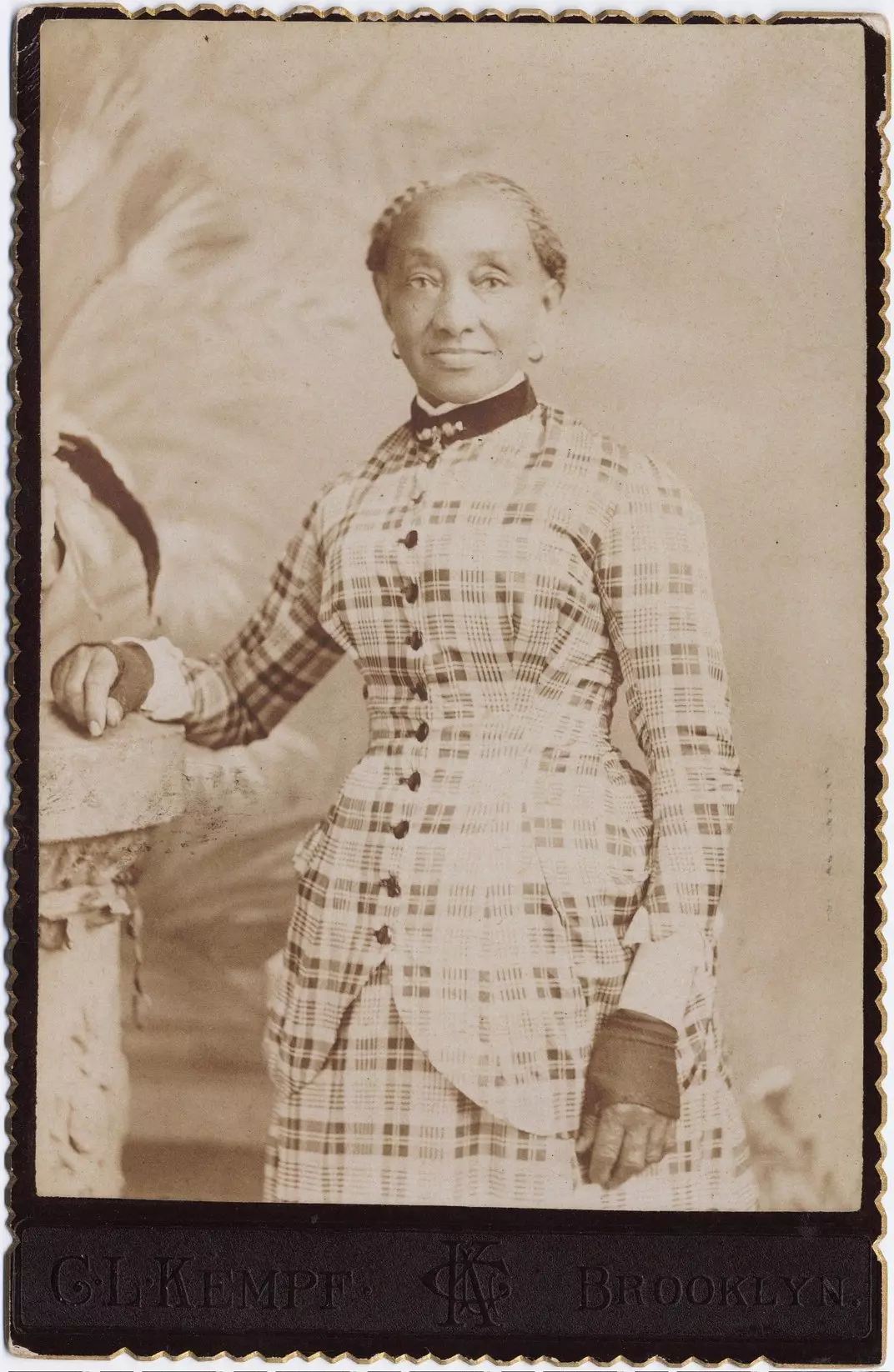 Tre fjärdedels längdporträtt av en äldre dam i en rutig klänning, cirka 1890