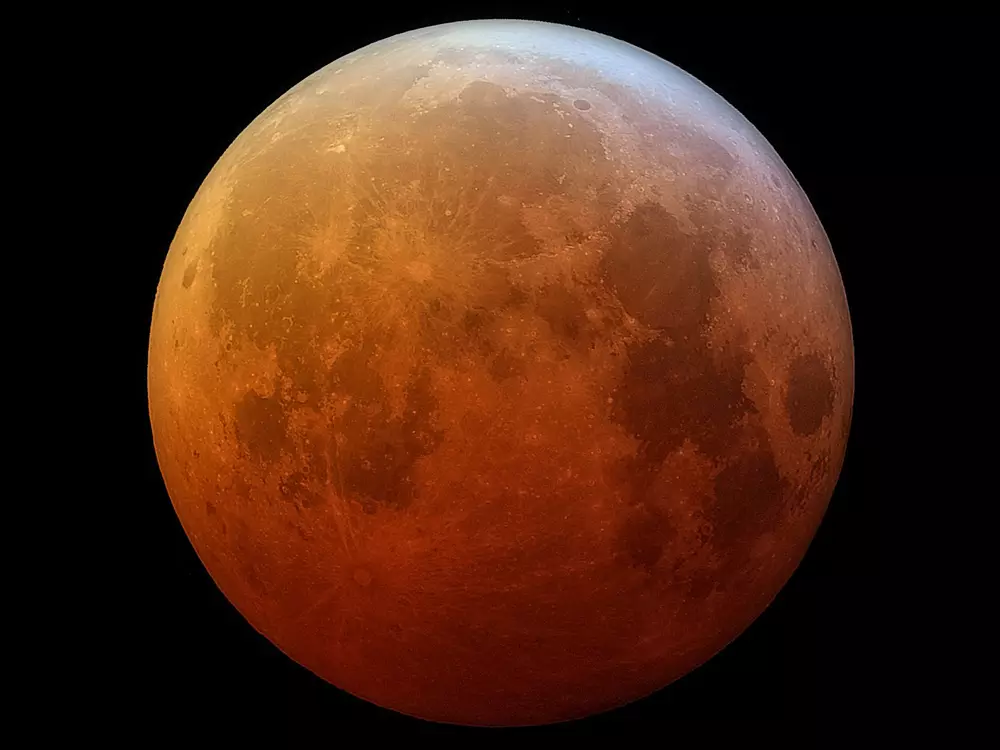 चंद्रग्रहणाचा एक फोटो जेथे चंद्र तळाशी लाल-केशरी दिसतो जो वरच्या बाजूस सामान्य राखाडी-पांढरा पर्यंत फिकट होतो