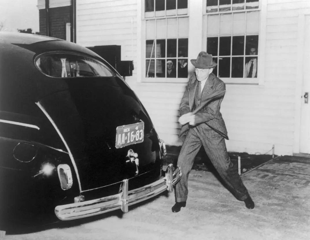 Henry Ford legănând un topor spre portbagajul de plastic al mașinii sale