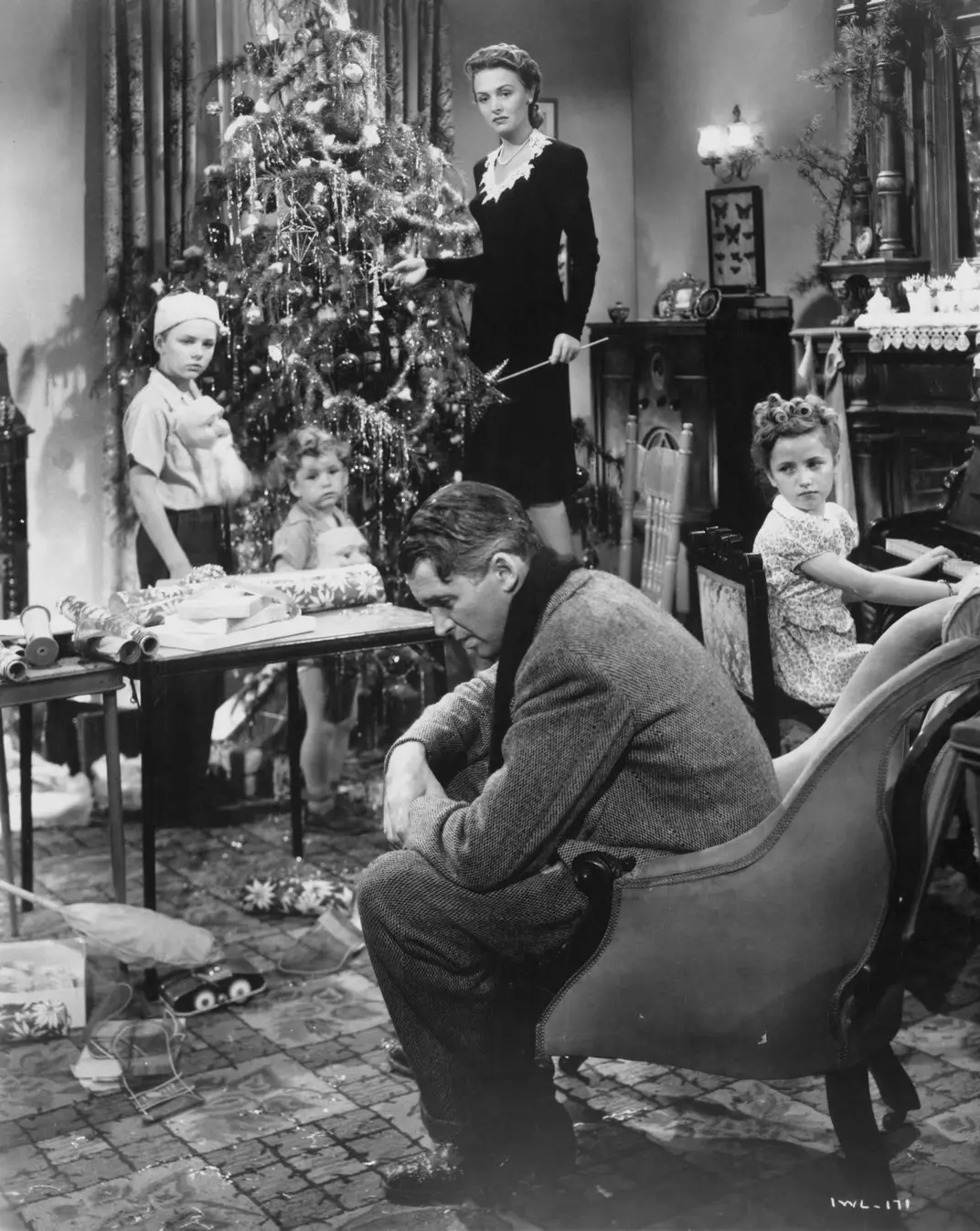 George Bailey sedí v kresle vo svojej obývačke, obklopený svojou manželkou a deťmi
