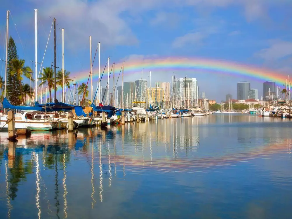 Foto de ĉielarko etendiĝanta trans Honolulu-haveno. La foto montras diversajn boatojn en la akvo kaj kaj spegulbildon de la ĉielarko en la akvo