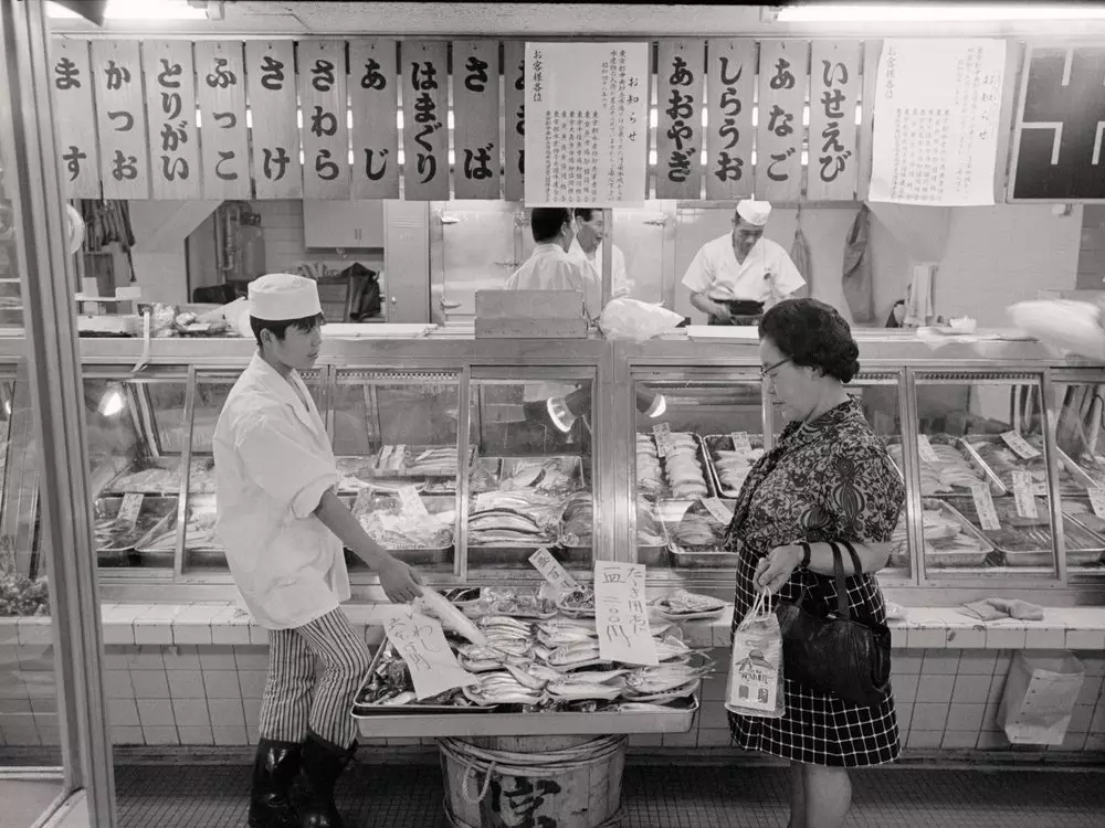 Kobieta wydaje się wahać, czy kupić ryby w sklepie w Tokio w 1973 roku
