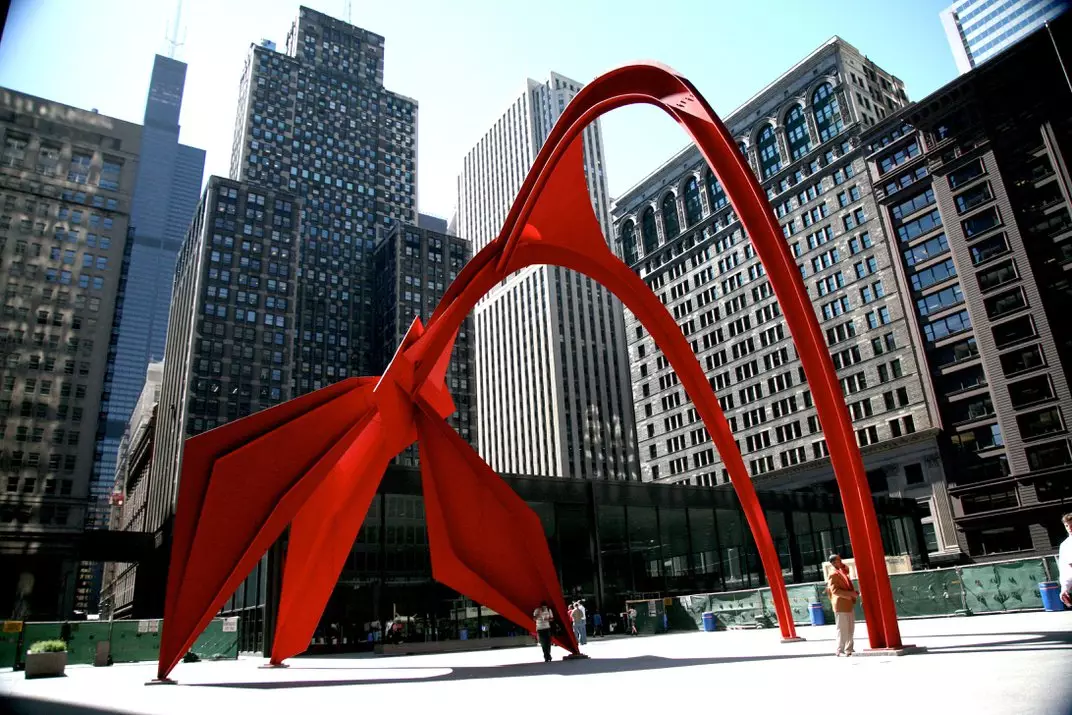 Uma escultura vermelha brilhante, enorme, eleva-se sobre uma praça; é composto por dois arcos longos e três arcos mais curtos agrupados na base