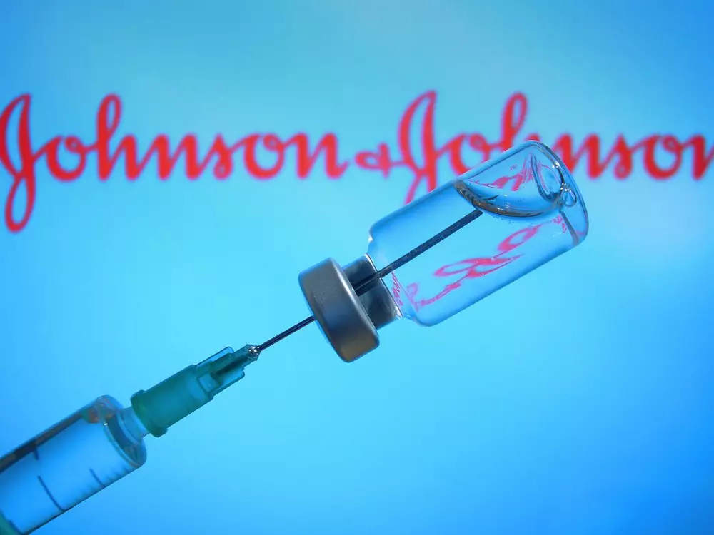 Вакцина Джонсон және Джонсон логотипі бар экранның алдында тұр