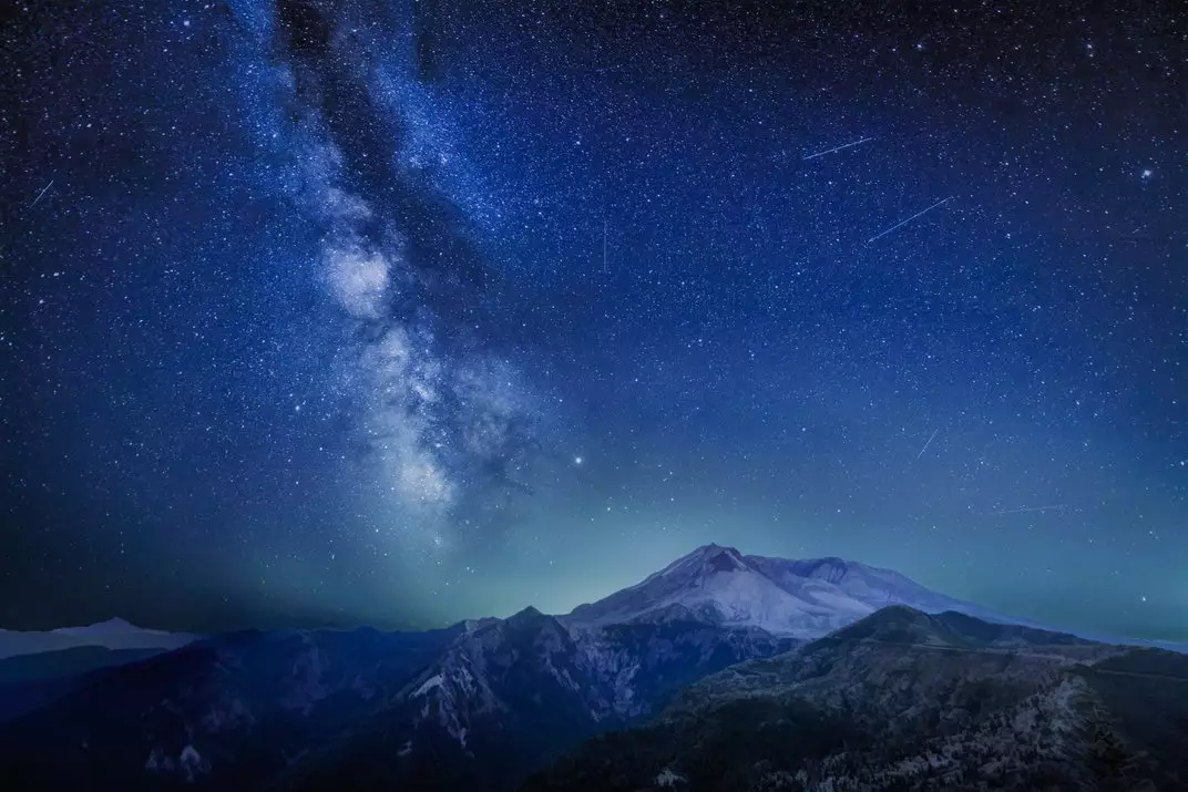 Melkeveien glitrer over en blågrønn himmel full av stjerneskudd, alt med utsikt over et hvitt fjell